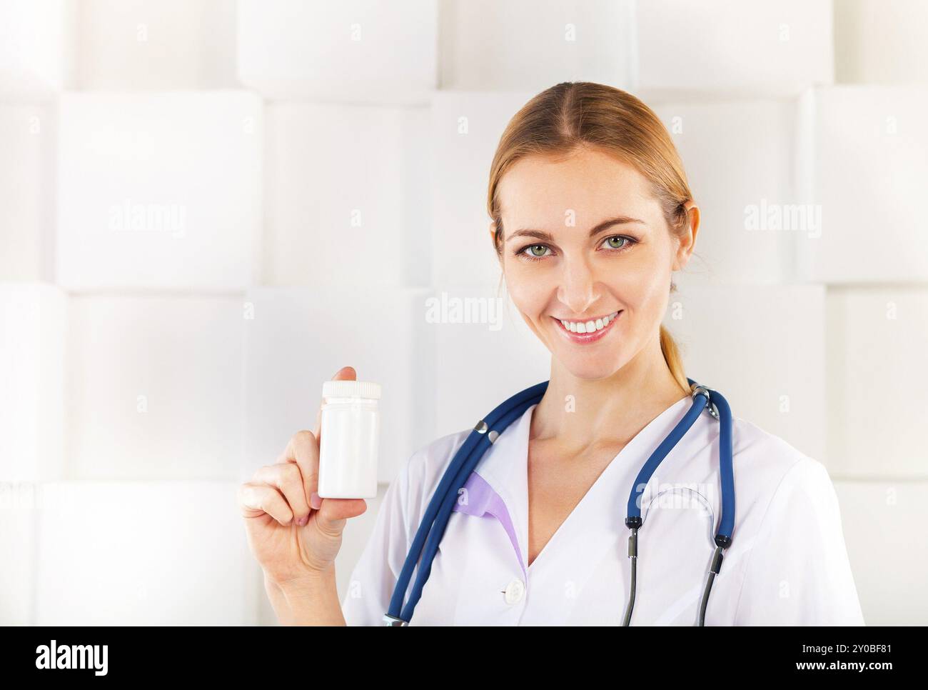 Pretty smiling woman doctor in uniform pointing a medicine bottle and ...