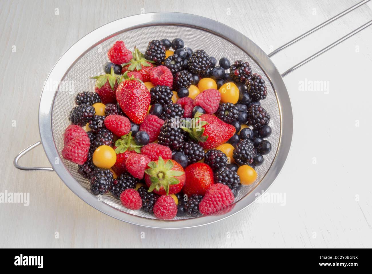 Mixed berries of different types, colors, and shapes in a colander ...