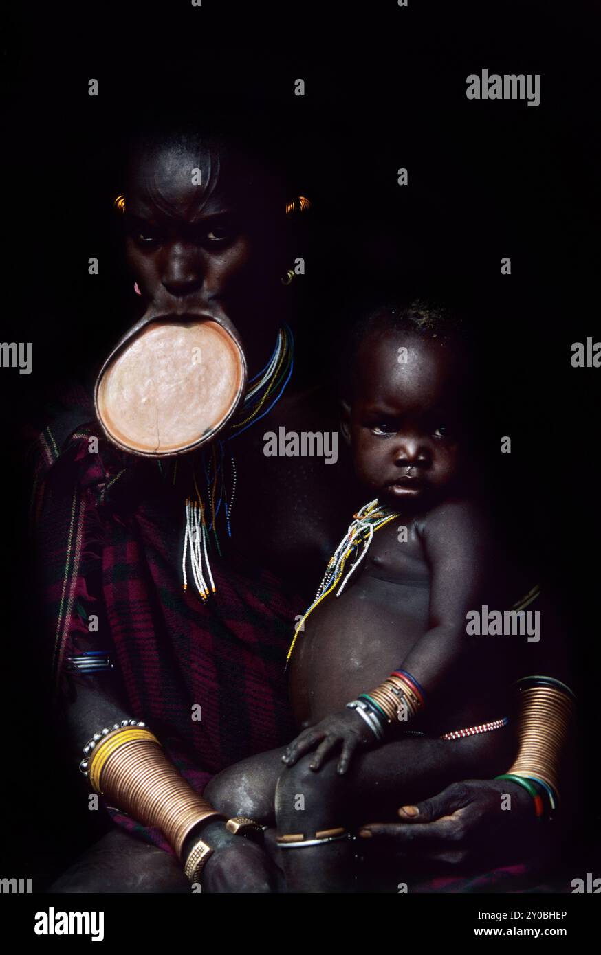 Portrait of a Surma woman and her child sitting in the door step of ...