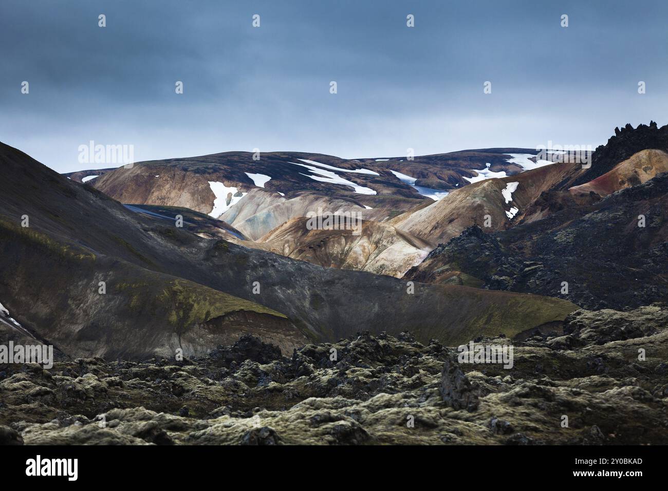 Gray moss covered lava in front of colorful mountains in ...