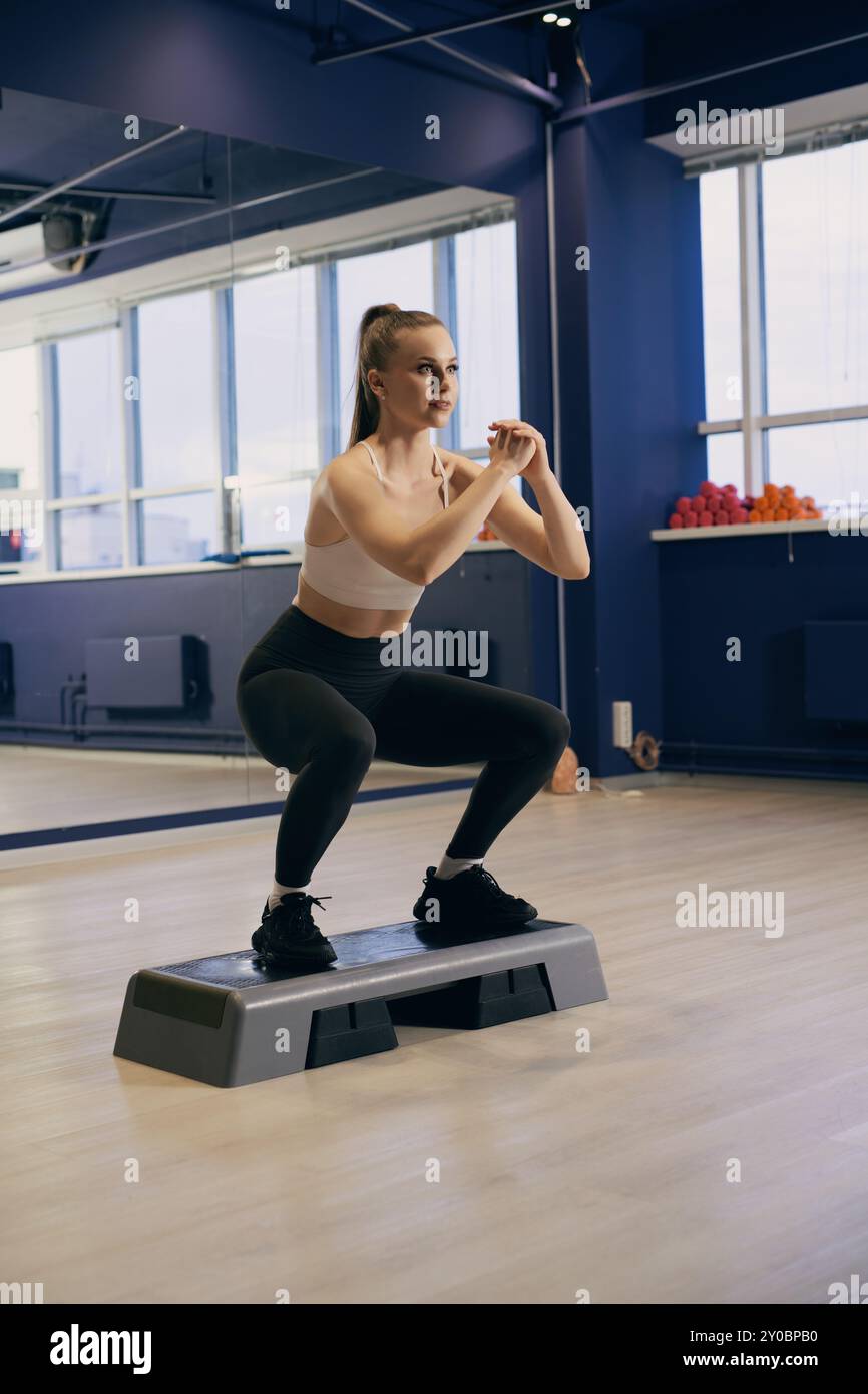 Woman performing squats on a step platform in a bright fitness studio ...