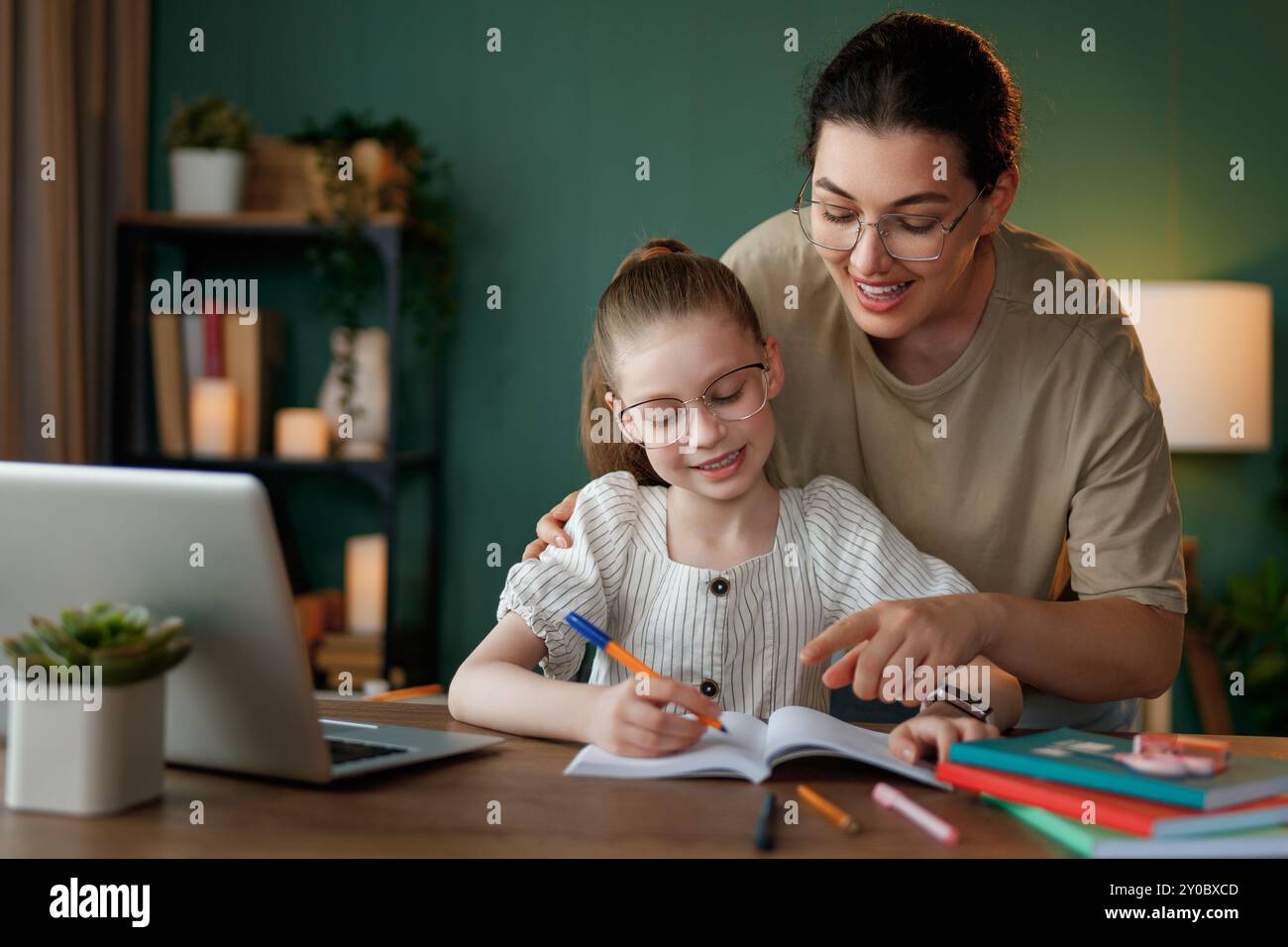 Happy child and adult are sitting at desk. Girl doing homework or ...