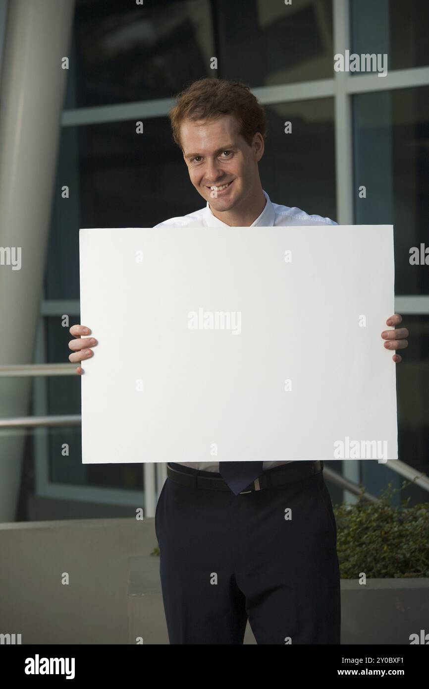 A happy and smiling office worker holding a blank sign outside of a ...