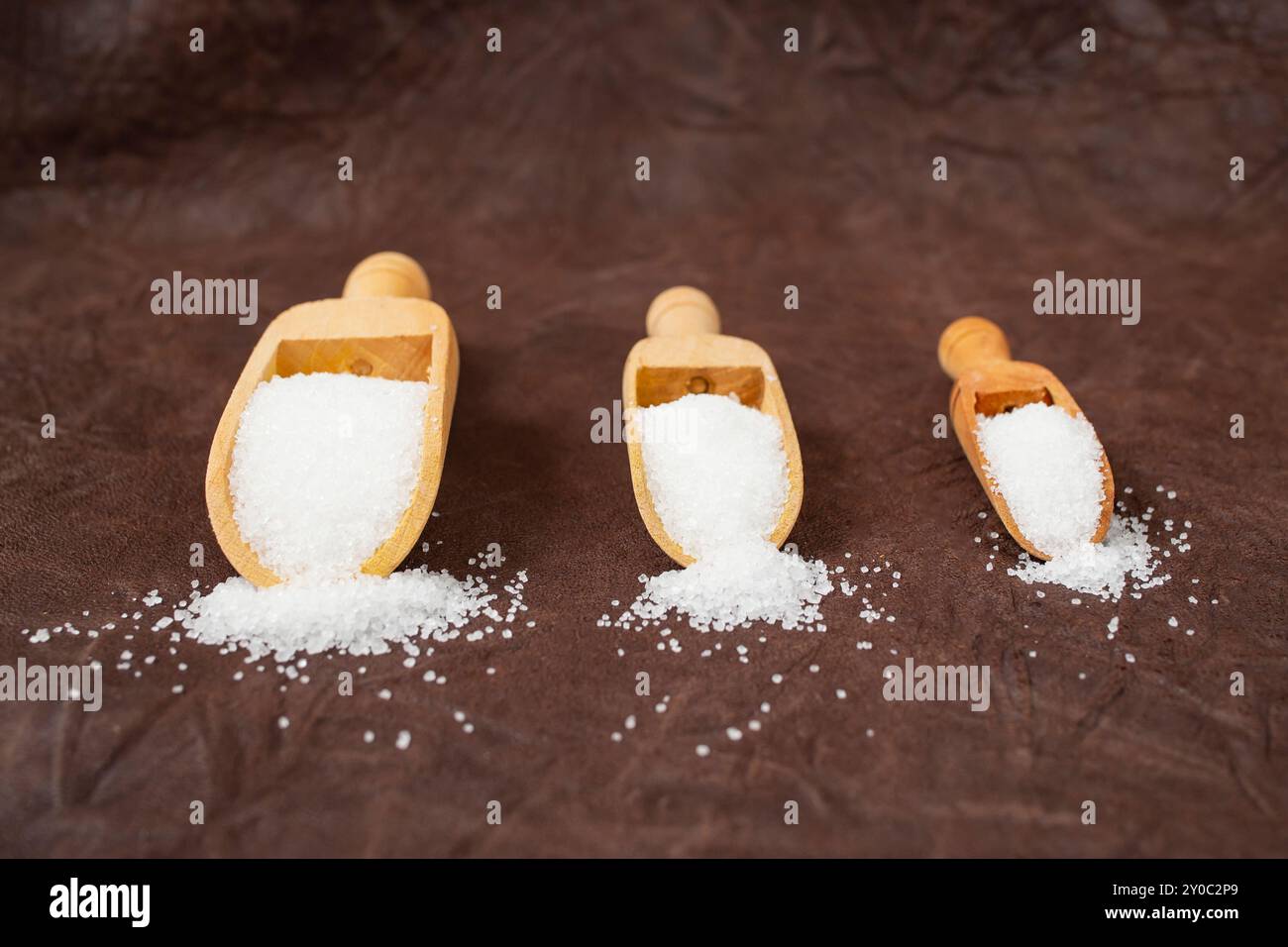 Three wooden scoops in different sizes full of white crystal sugar on ...