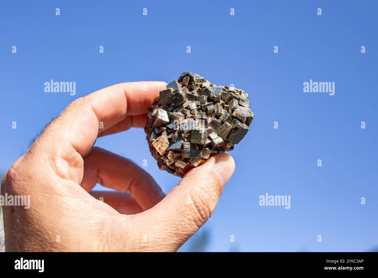 Male hand holding a golden mineral pyrite stone against blue sky, in ...