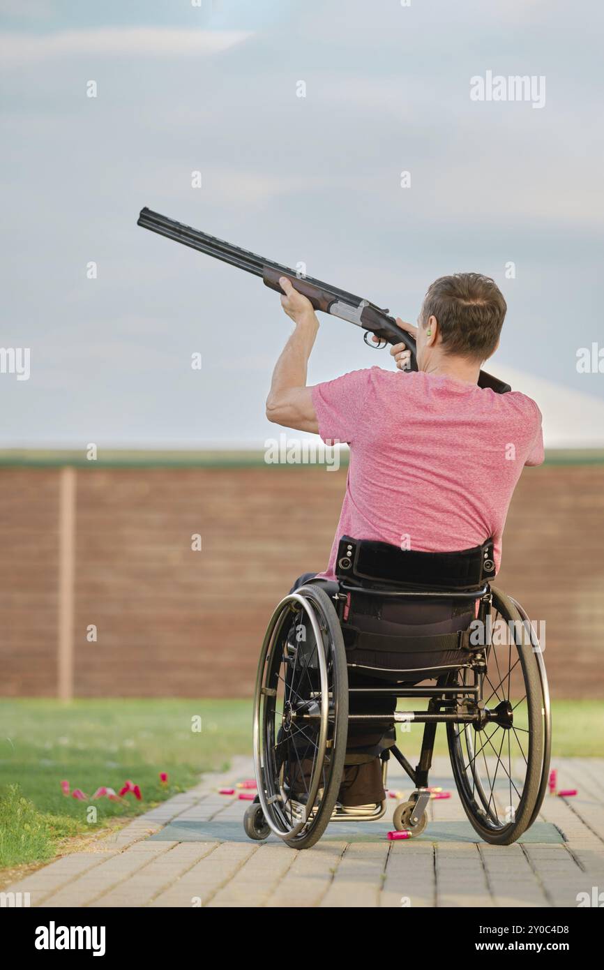 Rear view of a man in a wheelchair aiming at a clay pigeon at outdoor ...
