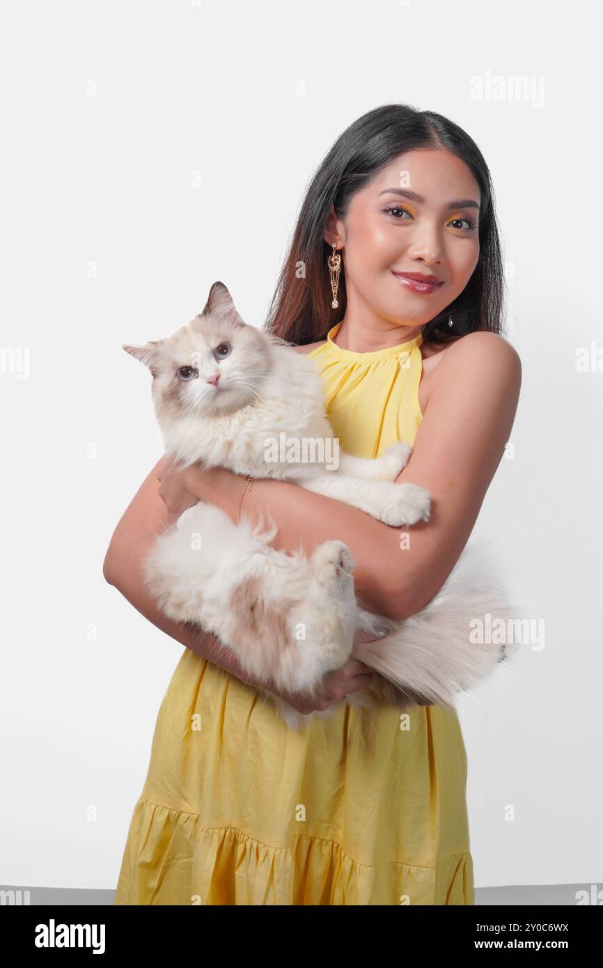 Smiling young Asian woman in yellow dress holding a white ragdoll cat ...