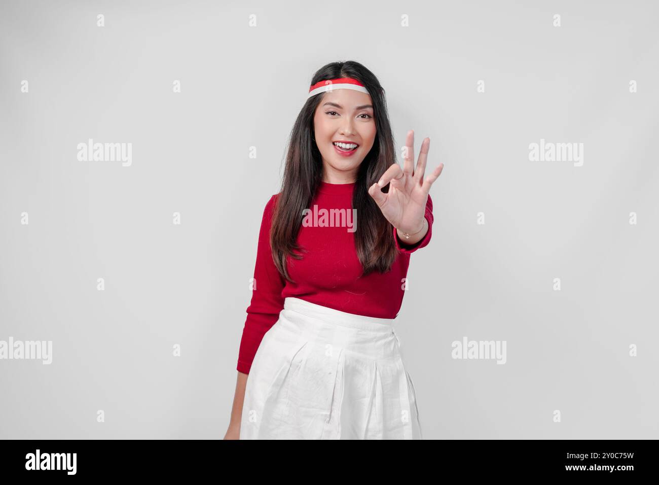 Happy young Asian woman in a red shirt and white skirt is giving okay ...