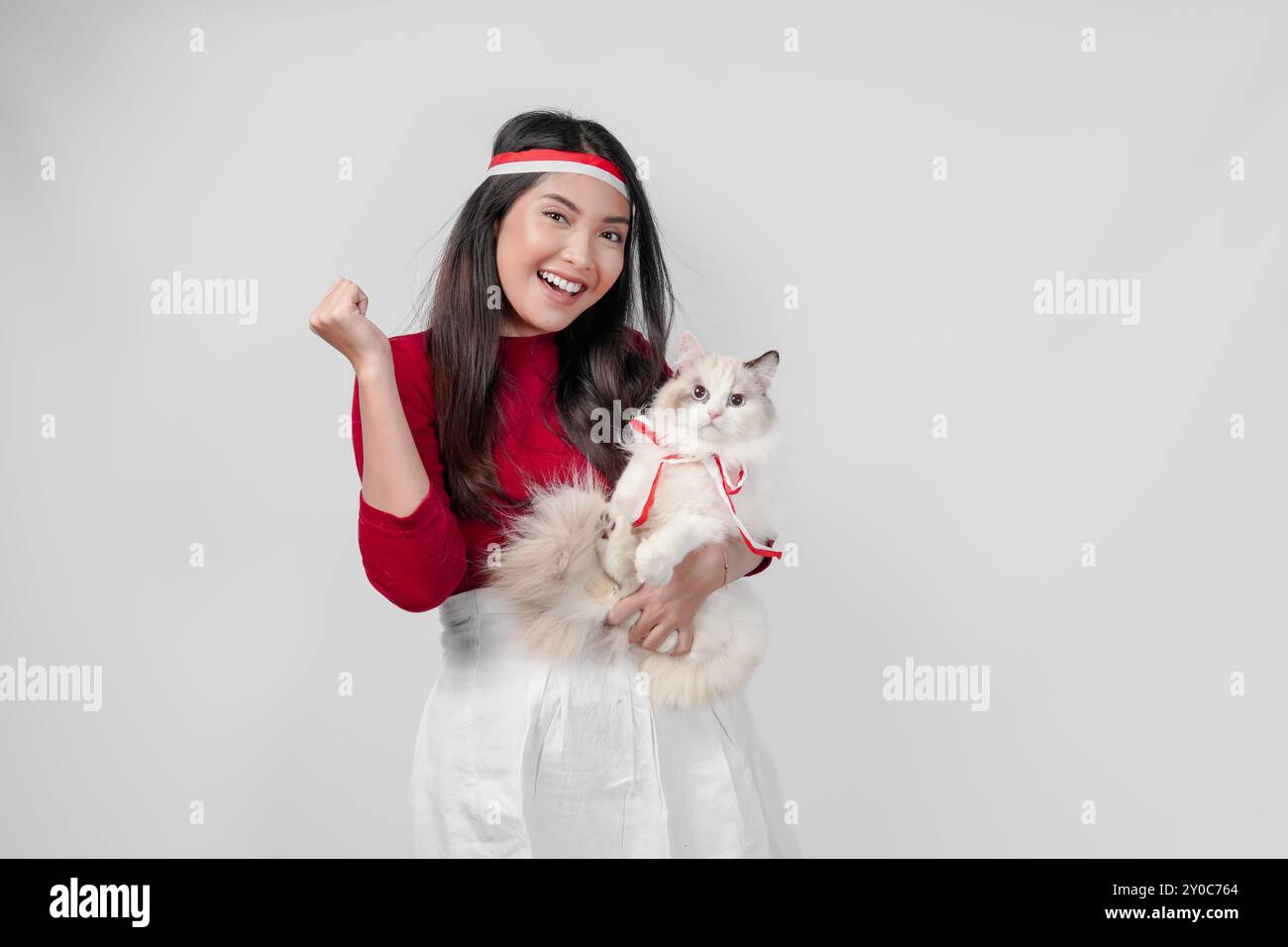 Smiling young Indonesian woman is holding a white ragdoll cat and ...