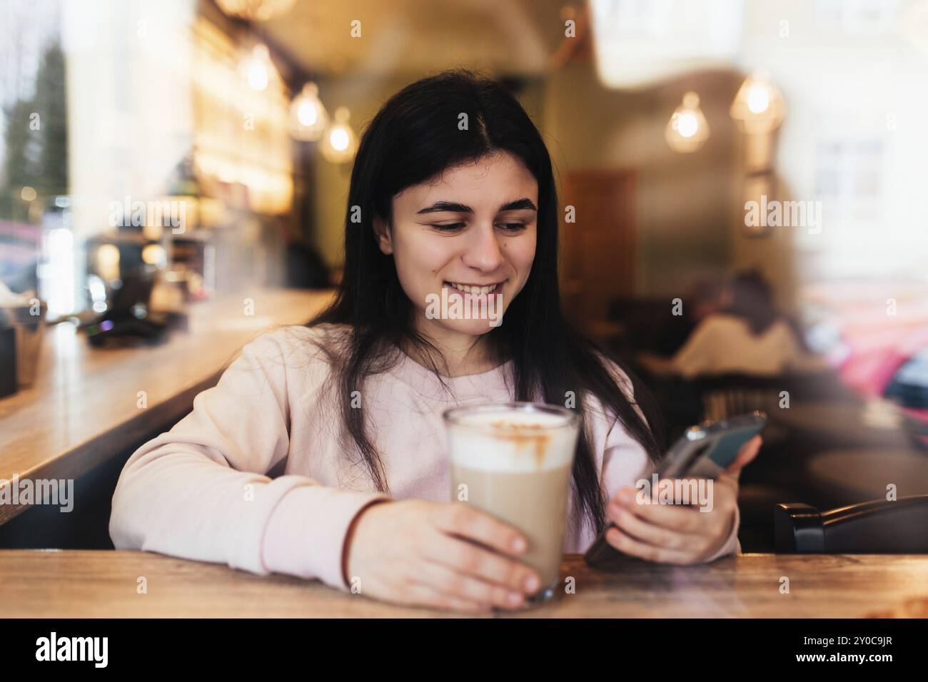 Girl smiling, drinks coffee in cafe and reading phone. Blurred ...