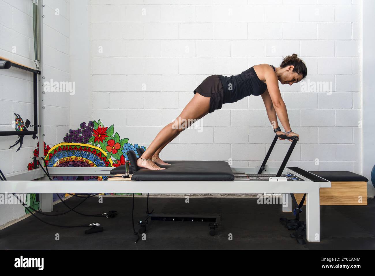 A woman doing a plank position on a Pilates reformer in a gym setting ...