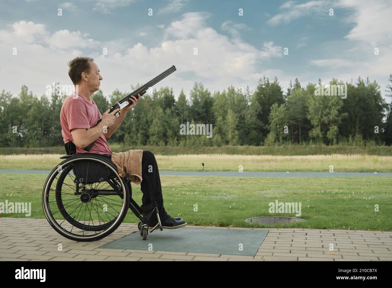 Side view of a determined old man using a wheelchair holding a rifle at ...