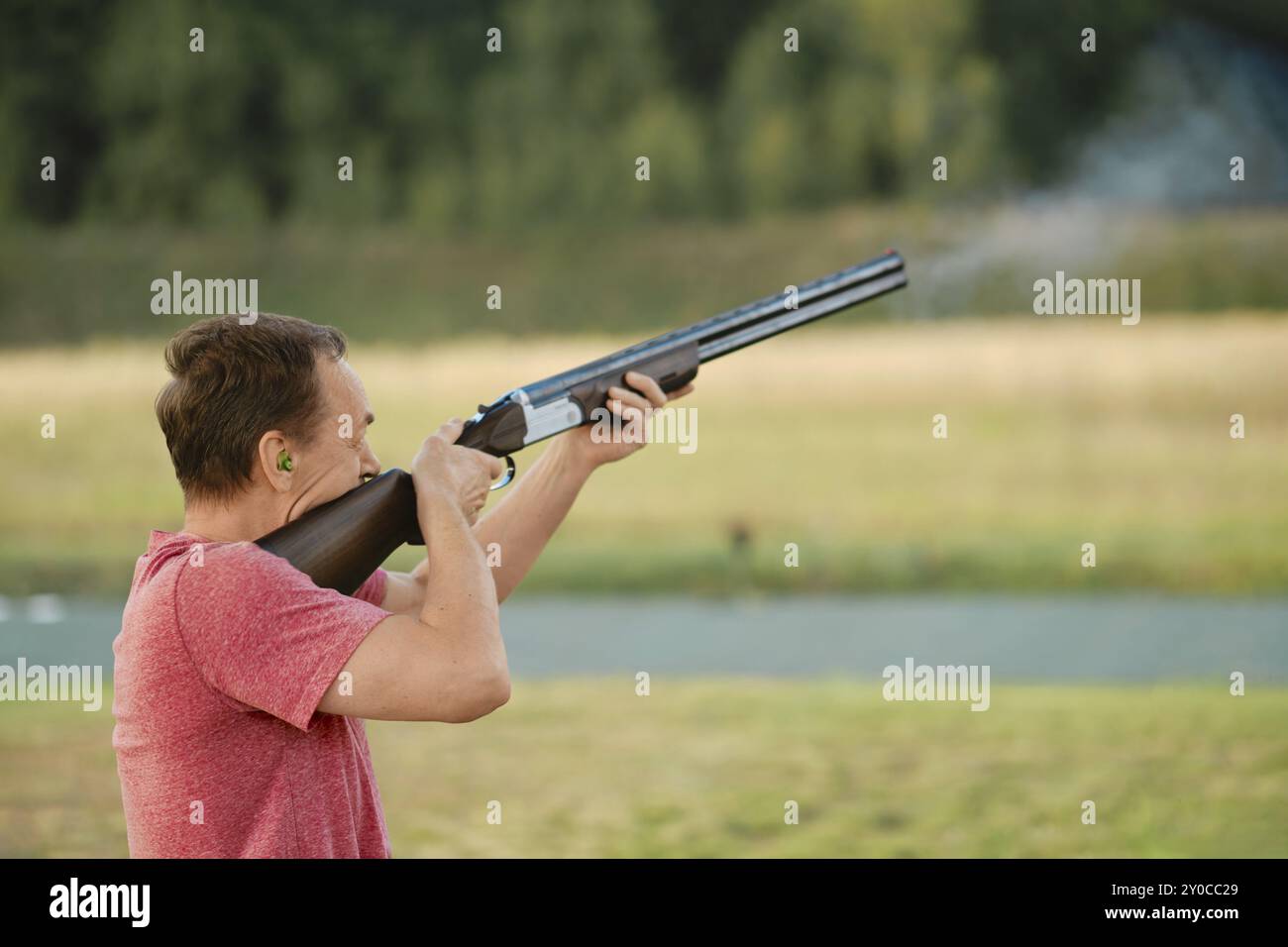 An old man shoots from a hunting rifle at a shooting range. Smoke from ...
