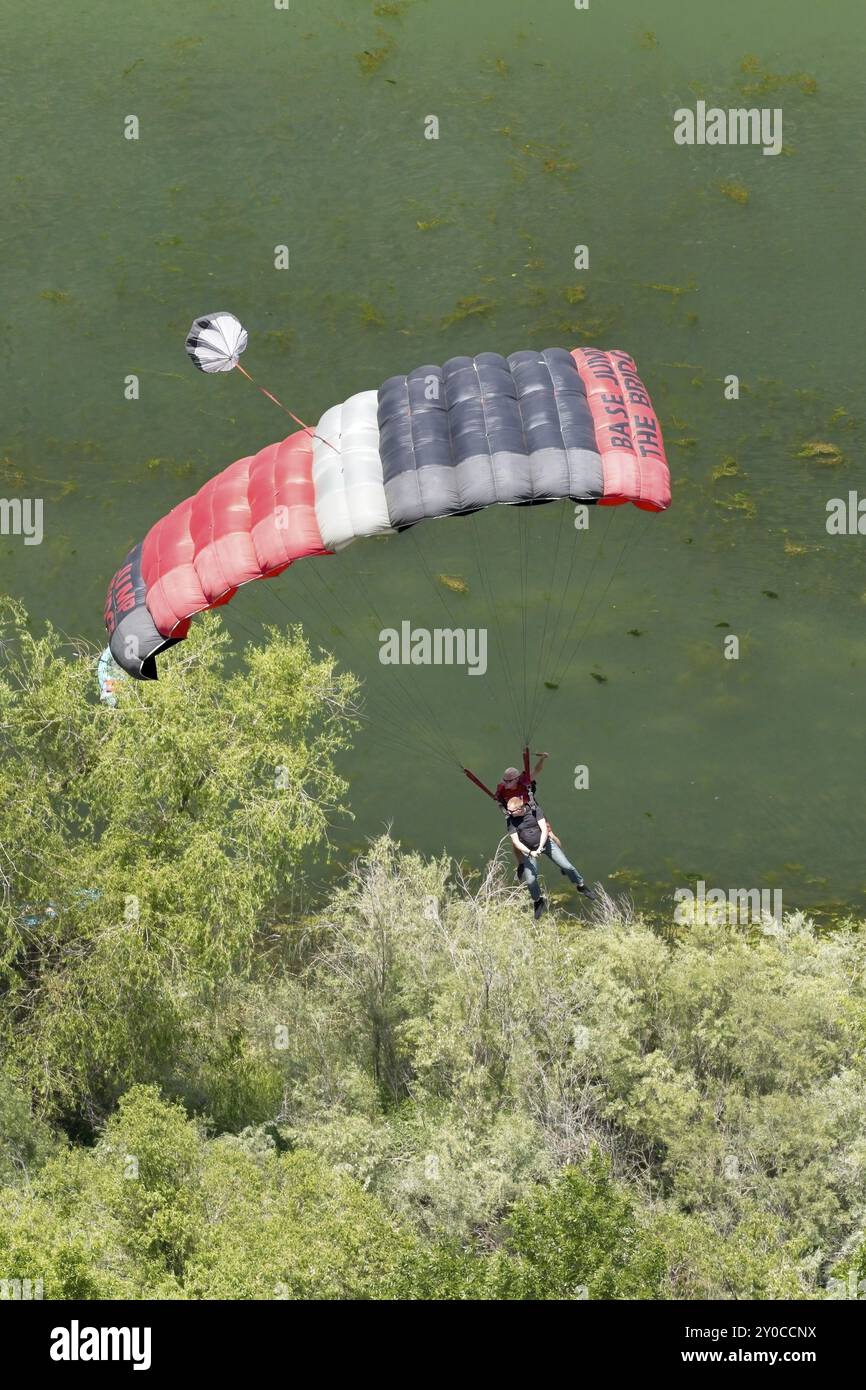 Tandem base jumpers soaring over the tree tops getting ready to land in ...