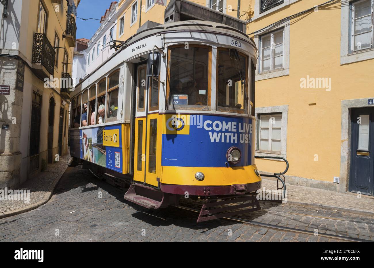 A yellow-blue tram winds its way through a cobbled street surrounded by ...