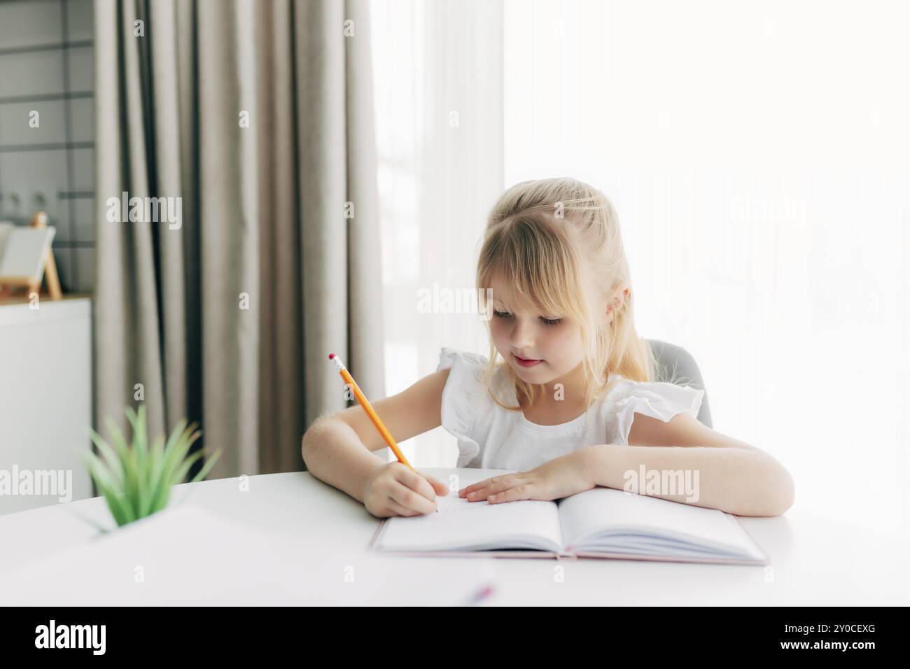 A little girl sits at the table and writes in a white notebook ...