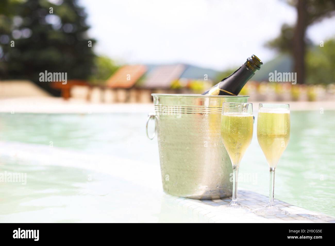 Champagne glasses and bottle in ice bucket near swimming pool. Vacation ...