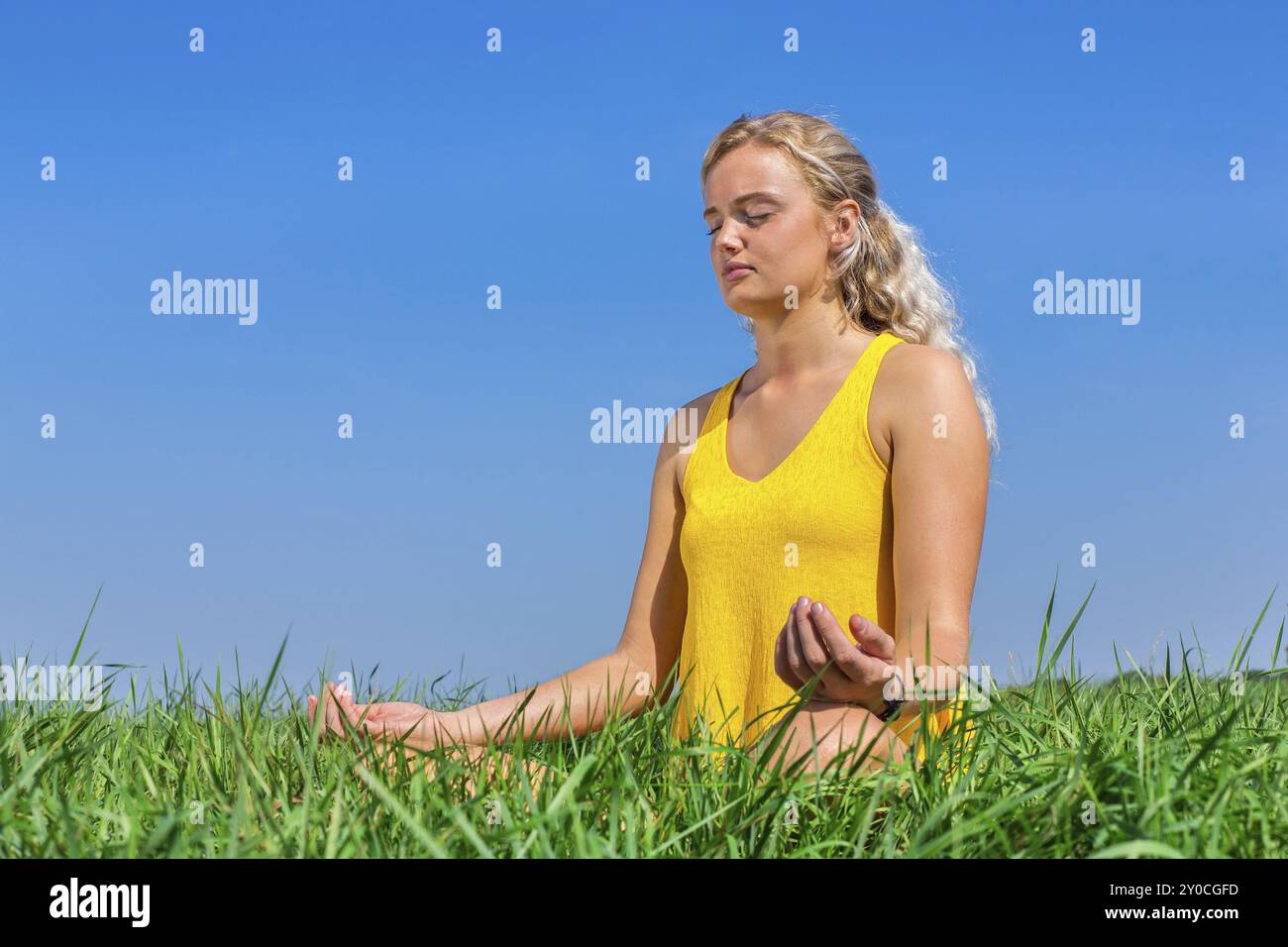 Young blond dutch woman meditating in nature with blue sky Stock Photo ...