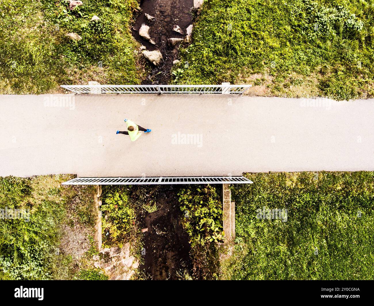 Aerial view of a runner running across bridge in park on a jogging path ...