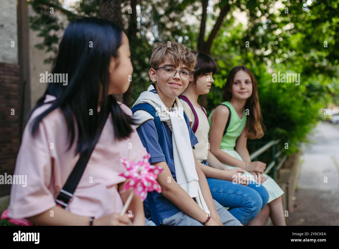 Four friends classmates sitting outdoors, waiting for bus Stock Photo ...
