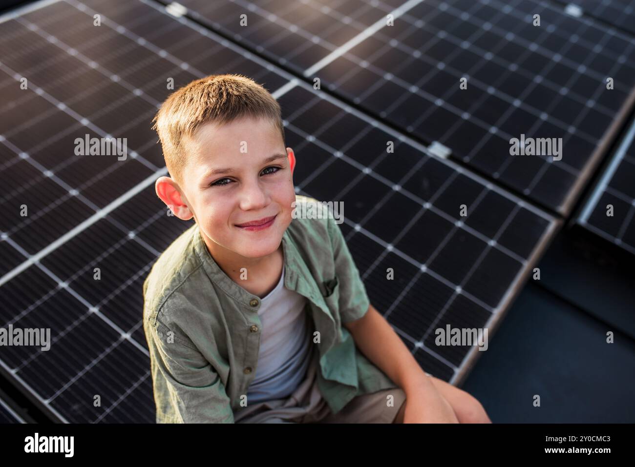 Cute boy sitting on roof with solar panels, looking at camera. Rooftop ...