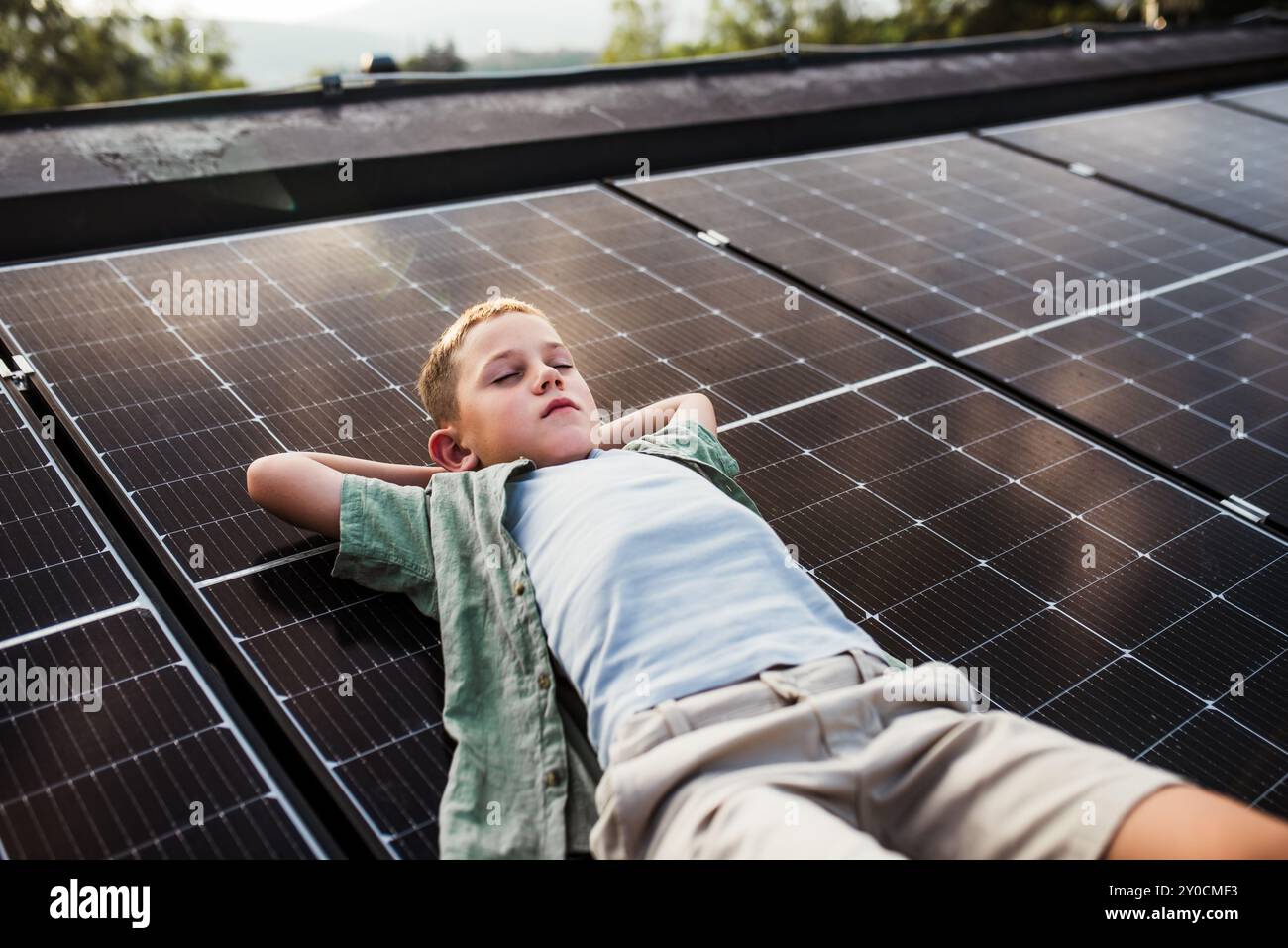 Boy lying on roof with solar panels, closed eyes. Rooftop solar or ...