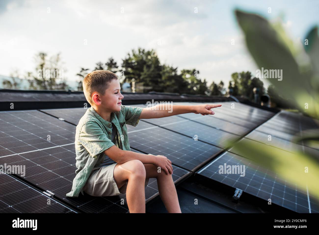 Cute boy sitting on roof with solar panels, looking at surrounding ...