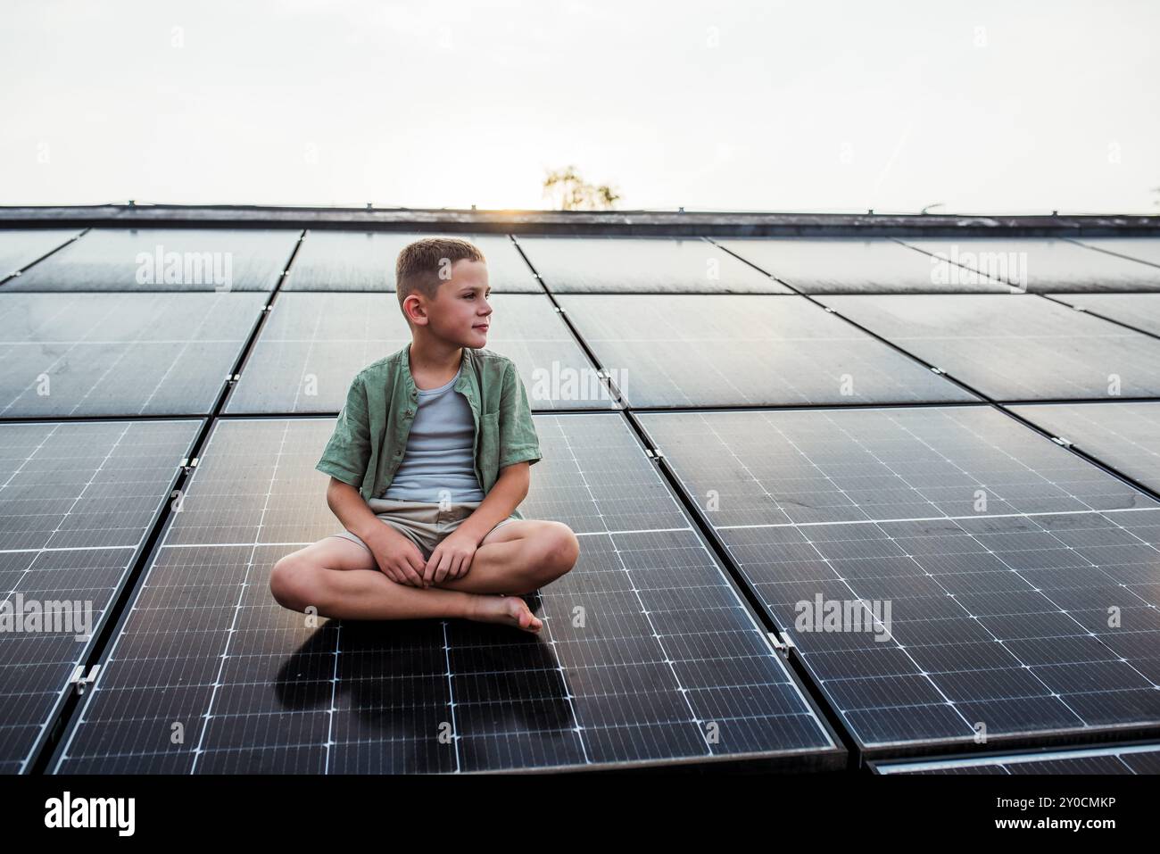 Cute boy sitting on roof with solar panels, looking at surrounding ...