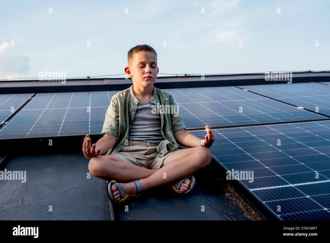 Cute boy sitting on roof with solar panels, meditating. Rooftop solar ...