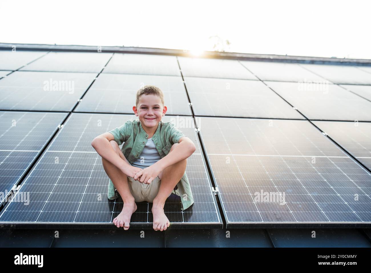 Cute boy sitting on roof with solar panels, looking at camera. Rooftop ...