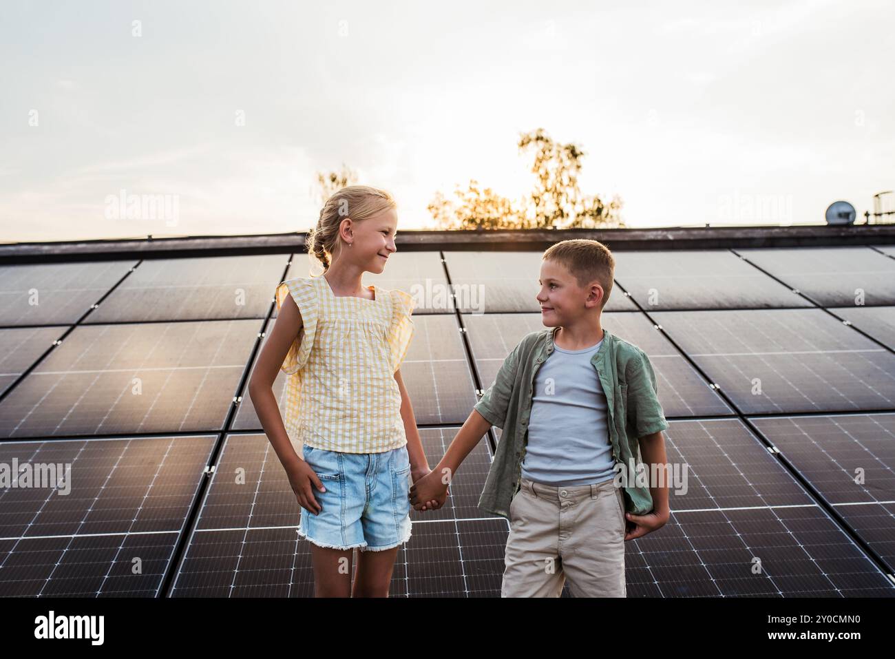 Two young siblings on roof with solar panels, looking at each other ...