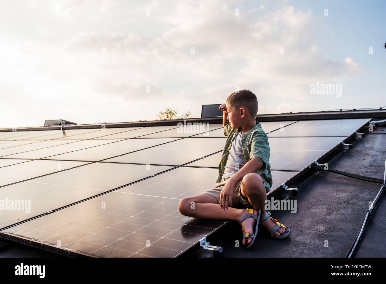 Cute boy sitting on roof with solar panels, looking at sunset. Rooftop ...
