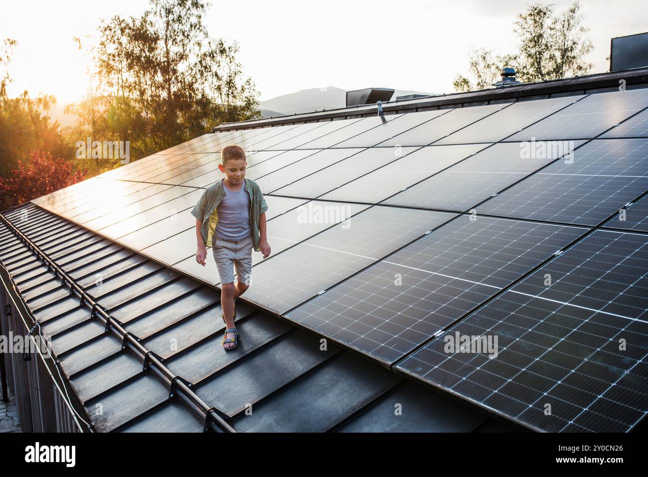 Boy walking on roof with solar panels during sunset, smiling, hands in ...