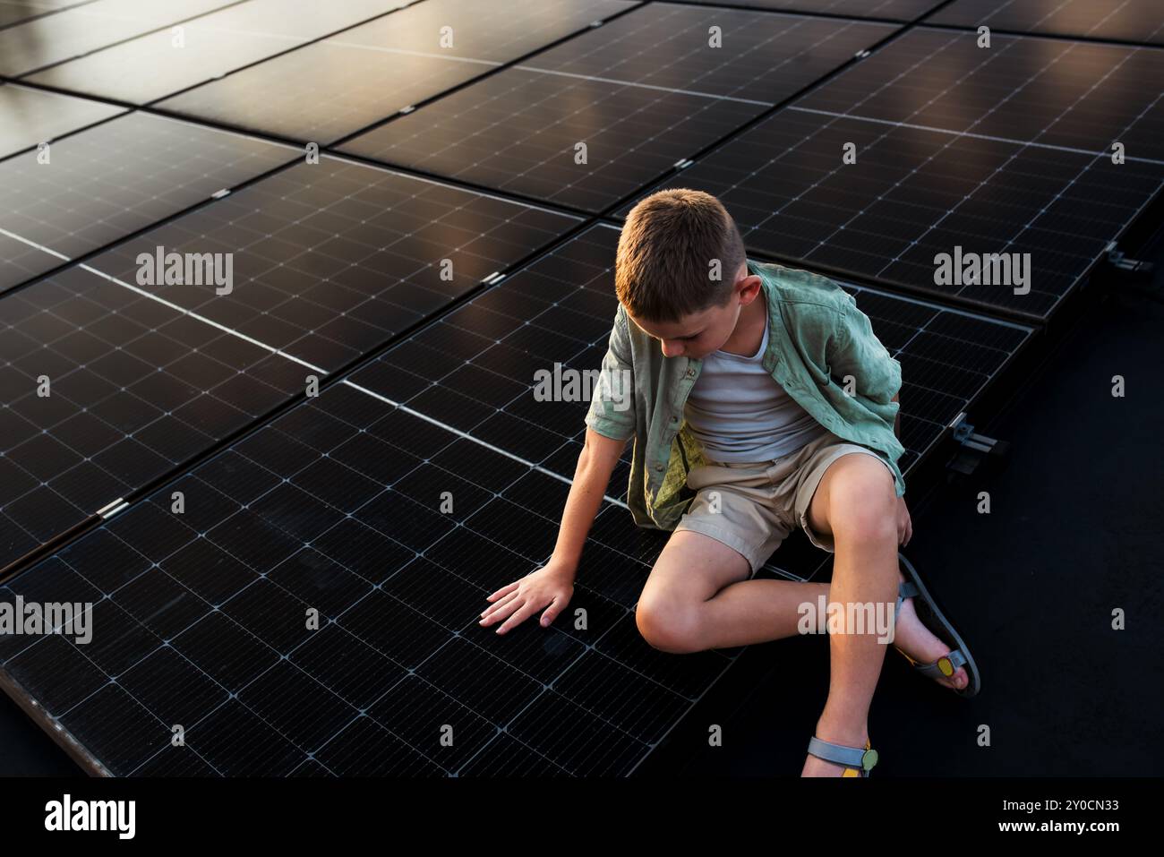 Boy sitting on roof with solar panels, touching panel with hands ...