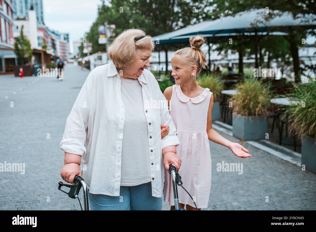 Grandma with walker and granddaugter in the city, on walk. Girl ...