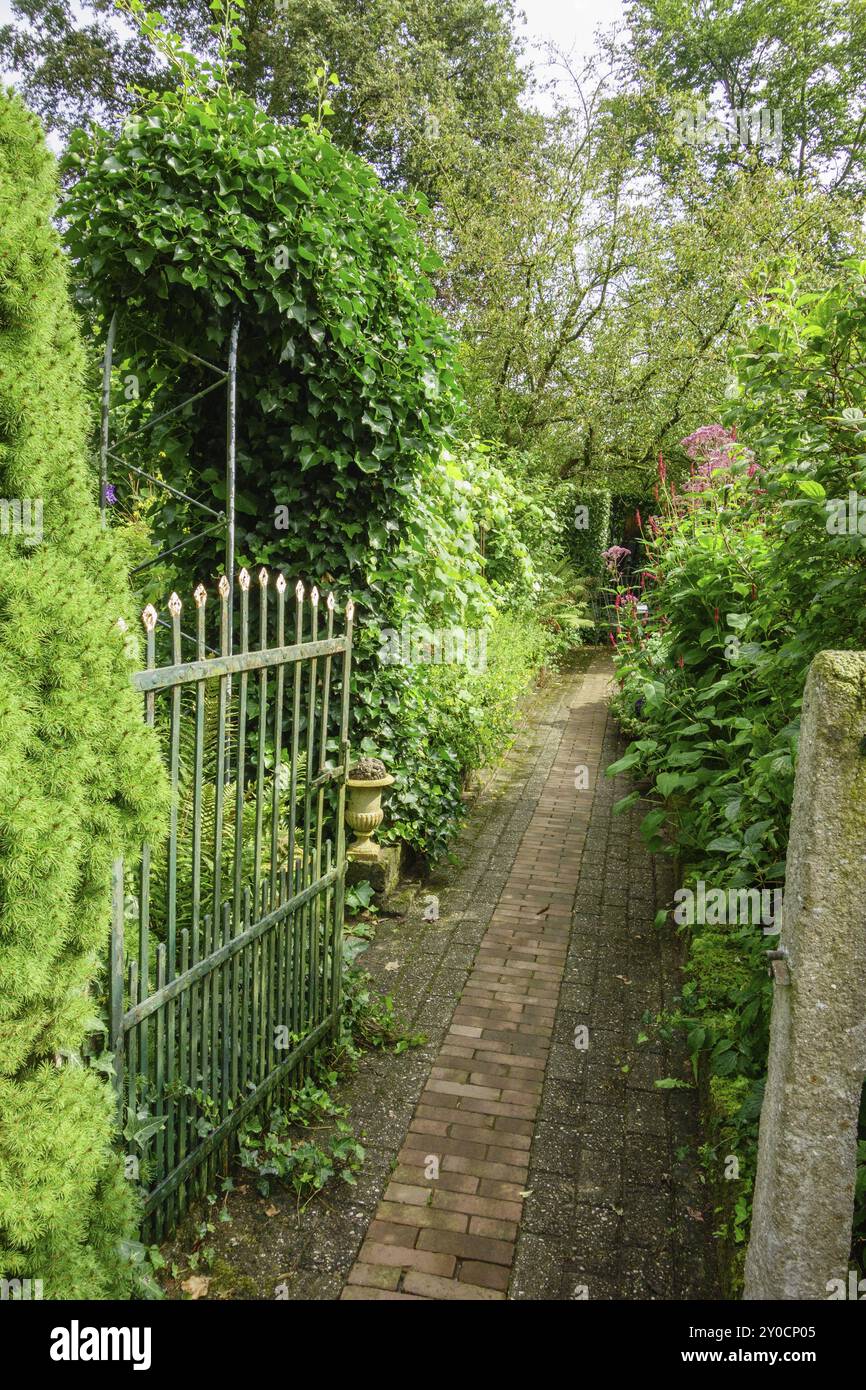 A narrow cobblestone path leading through a gate into a lushly planted ...
