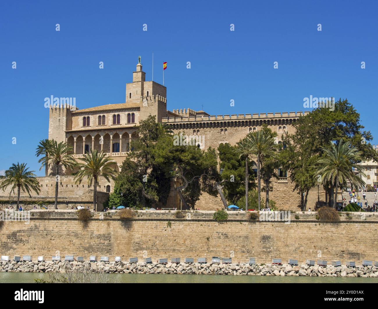 A castle with a stone wall and palm trees in summer under a blue sky ...