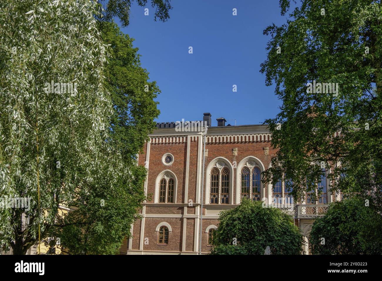 Historic brick building with large windows surrounded by green trees ...