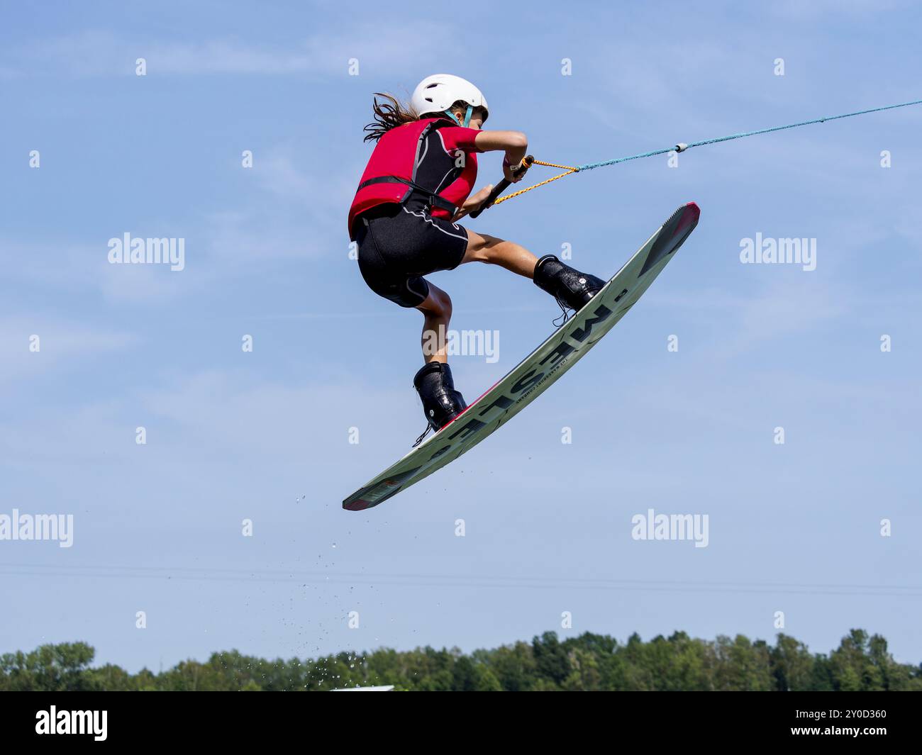 Boy or girl jumping with wakeboard, red life jacket, water sports ...