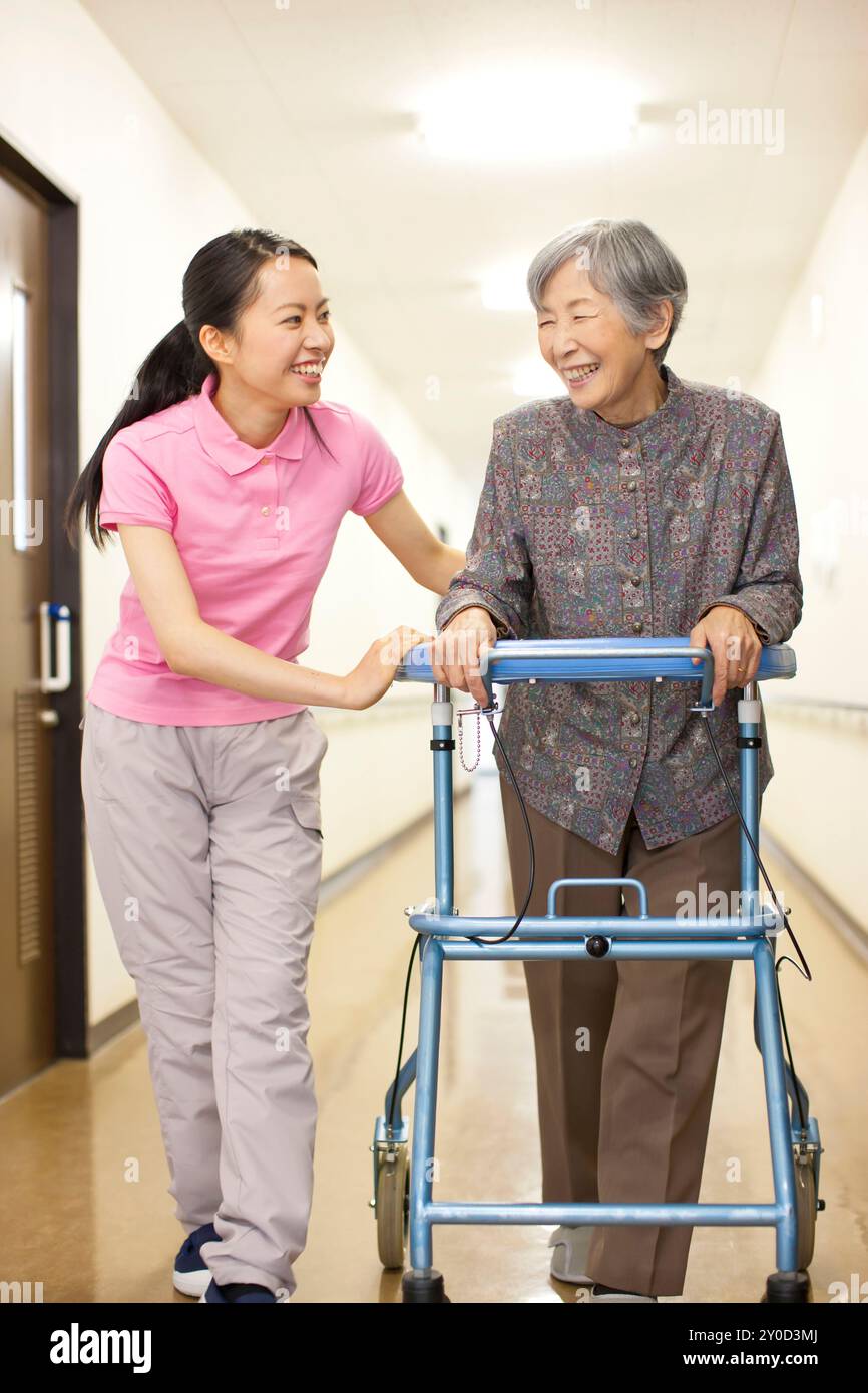 An elderly woman undergoing gait training with a woman caregiver by her ...