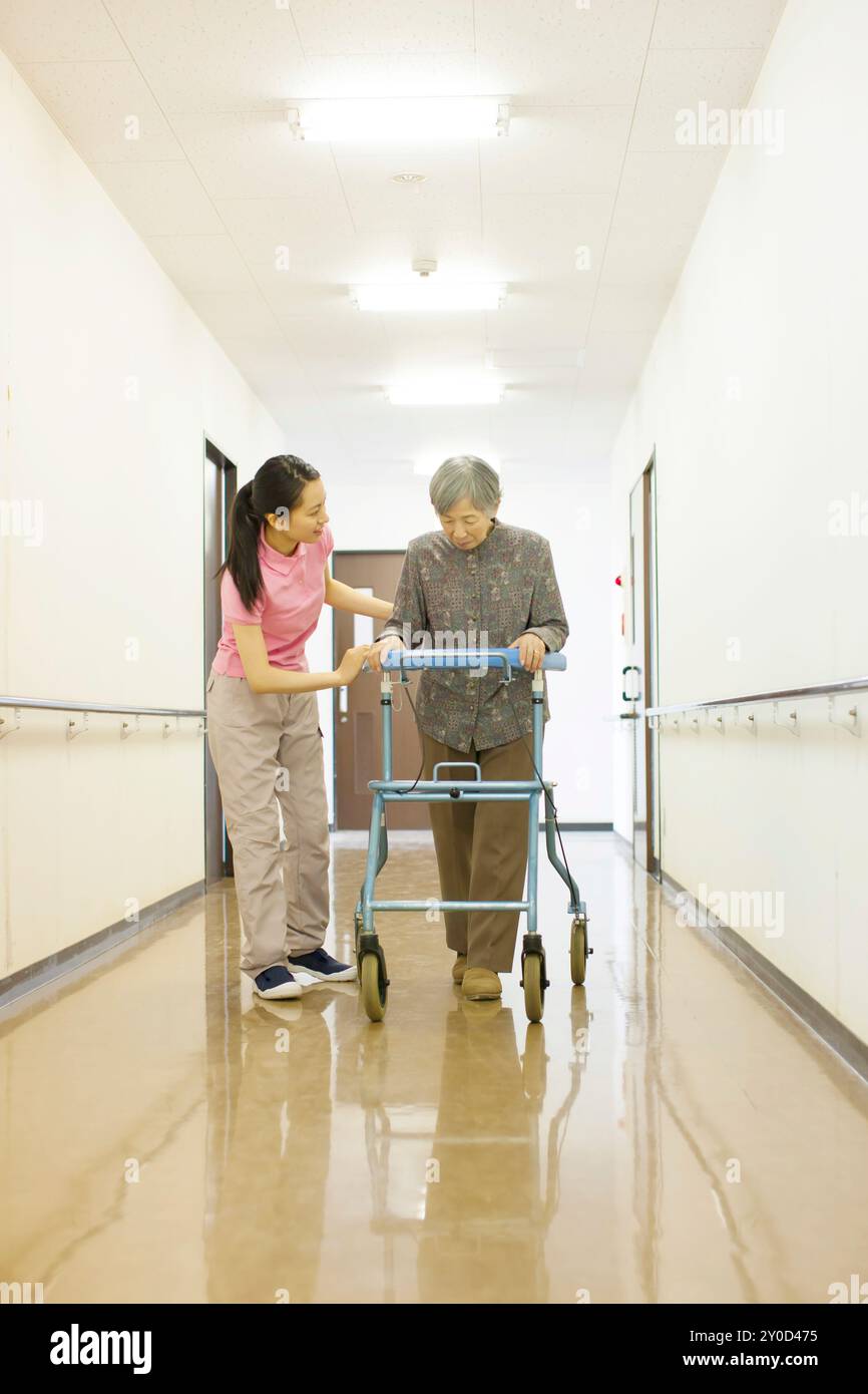 An elderly woman undergoing gait training with a woman caregiver by her ...