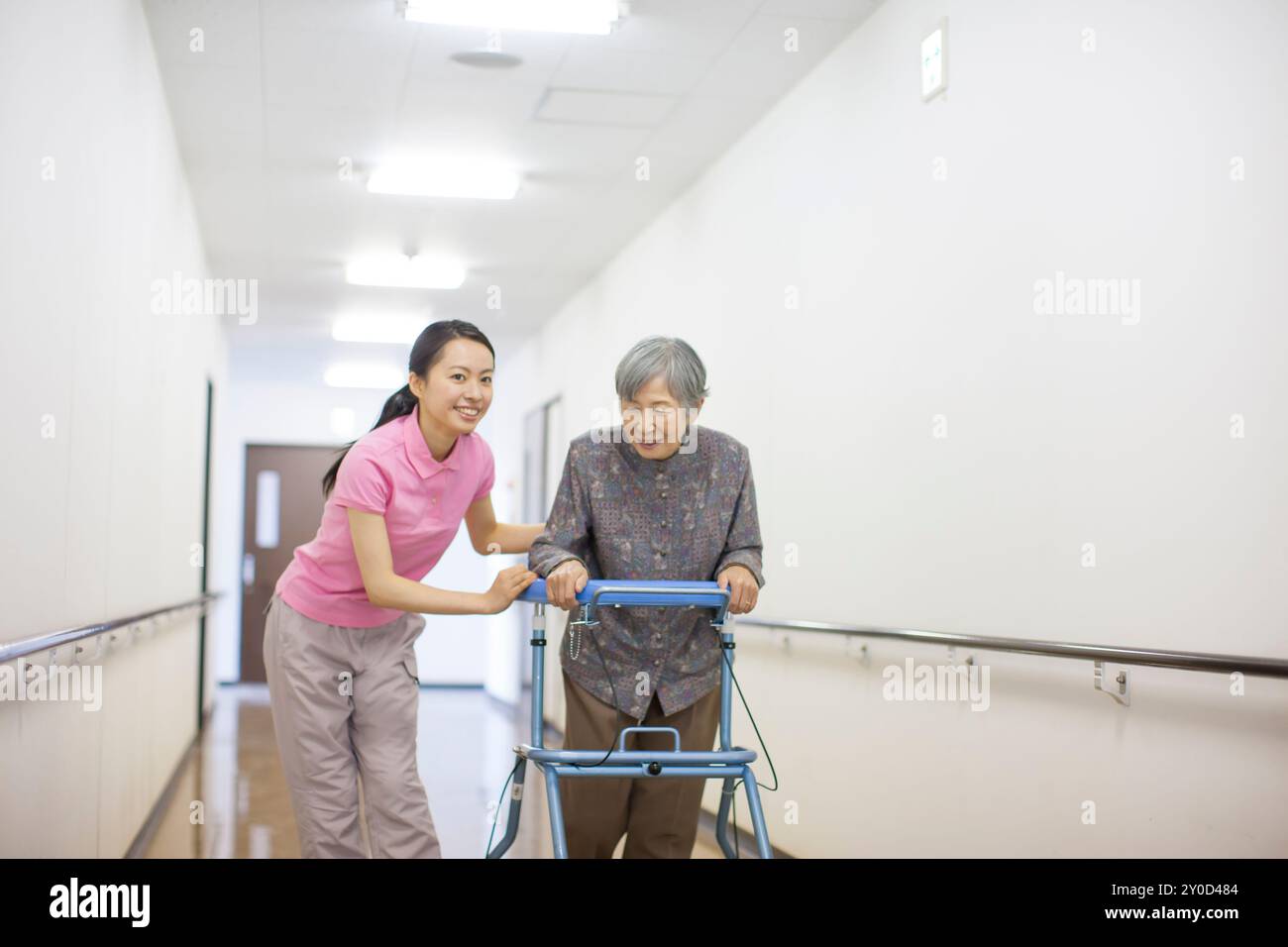 An elderly woman undergoing gait training with a woman caregiver by her ...