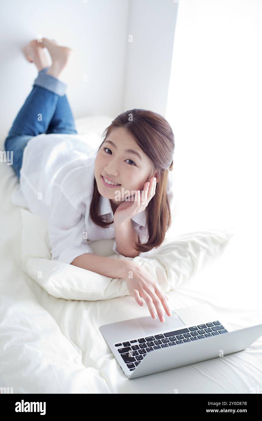 A woman operating a computer lying down on a bed Stock Photo - Alamy
