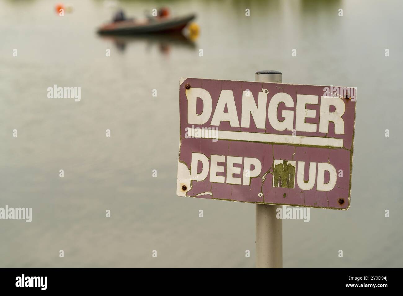 Sign: Danger, deep mud, with a boat in the blurry background, seen in ...