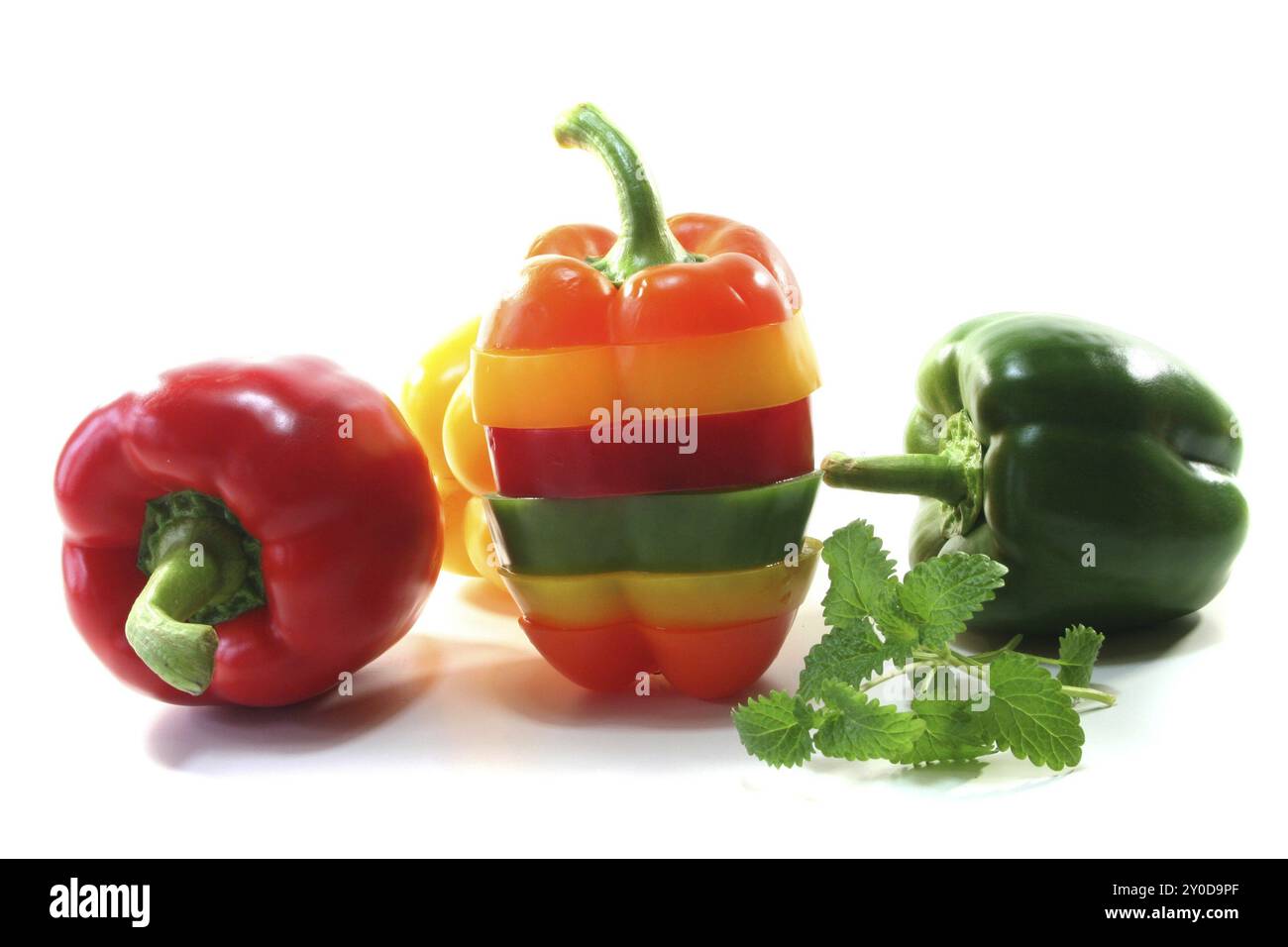 Different coloured peppers layered with lemon balm on a white ...