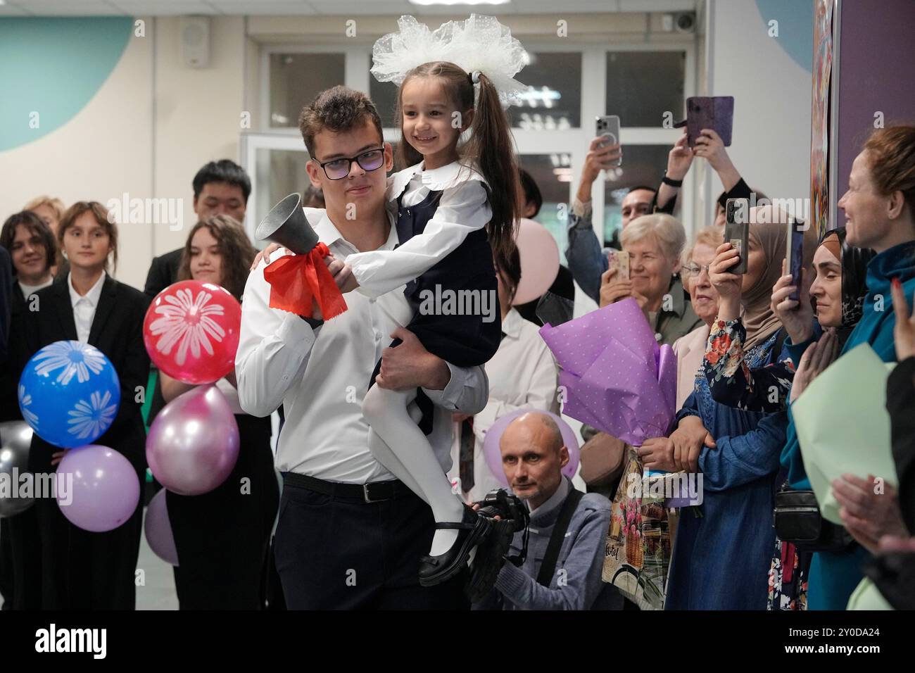 A first grader and a high school student ring a bell during a ceremony ...