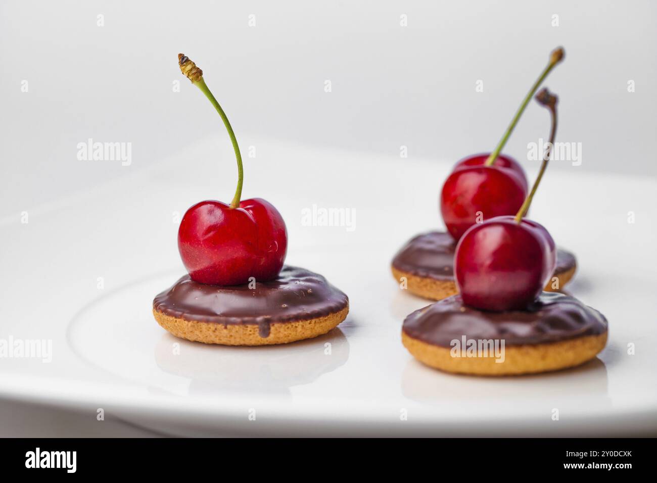Three cherries on three chocolate biscuits Stock Photo - Alamy