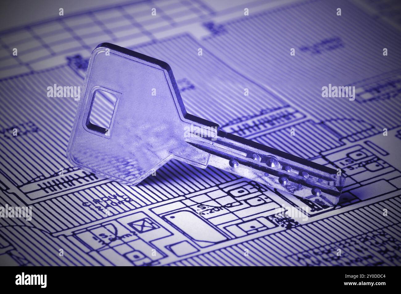 A key rests on top of a house blueprint. The overall image tone is blue ...