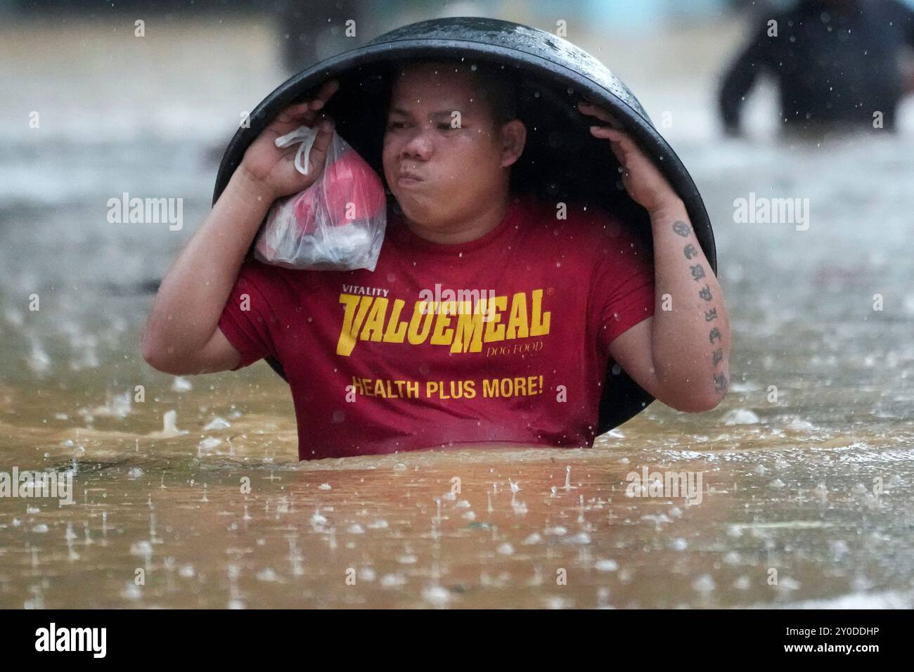 A resident uses a laundry tub to protect him from rain as he wades ...