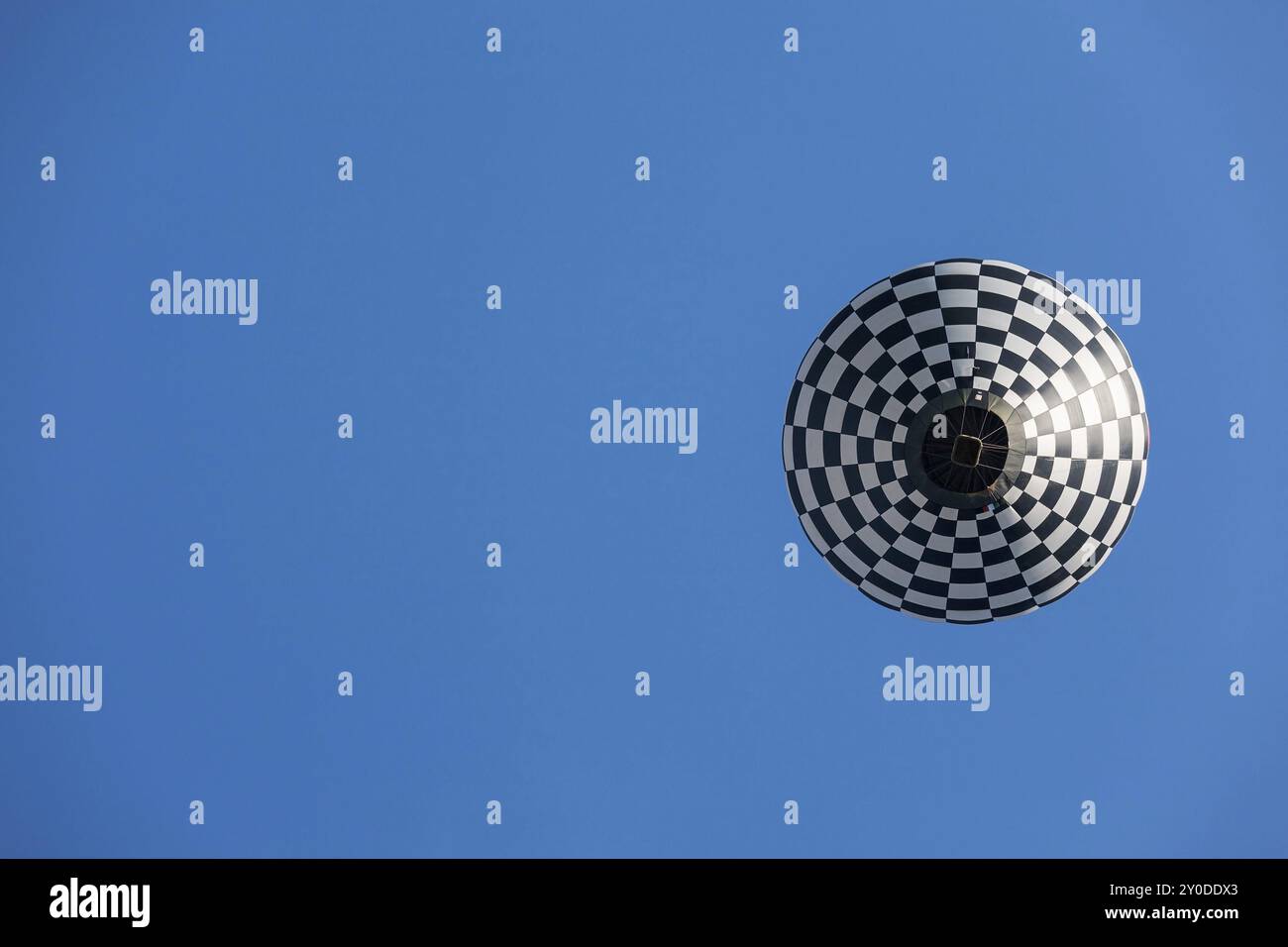 Black and white balloon in flight seen from below against a blue sky ...